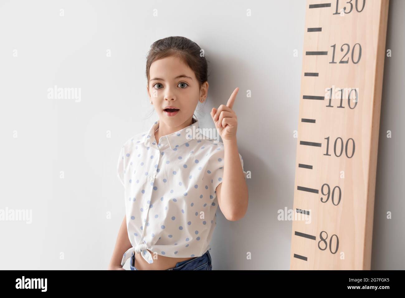 Little girl measuring height near light wall Stock Photo - Alamy
