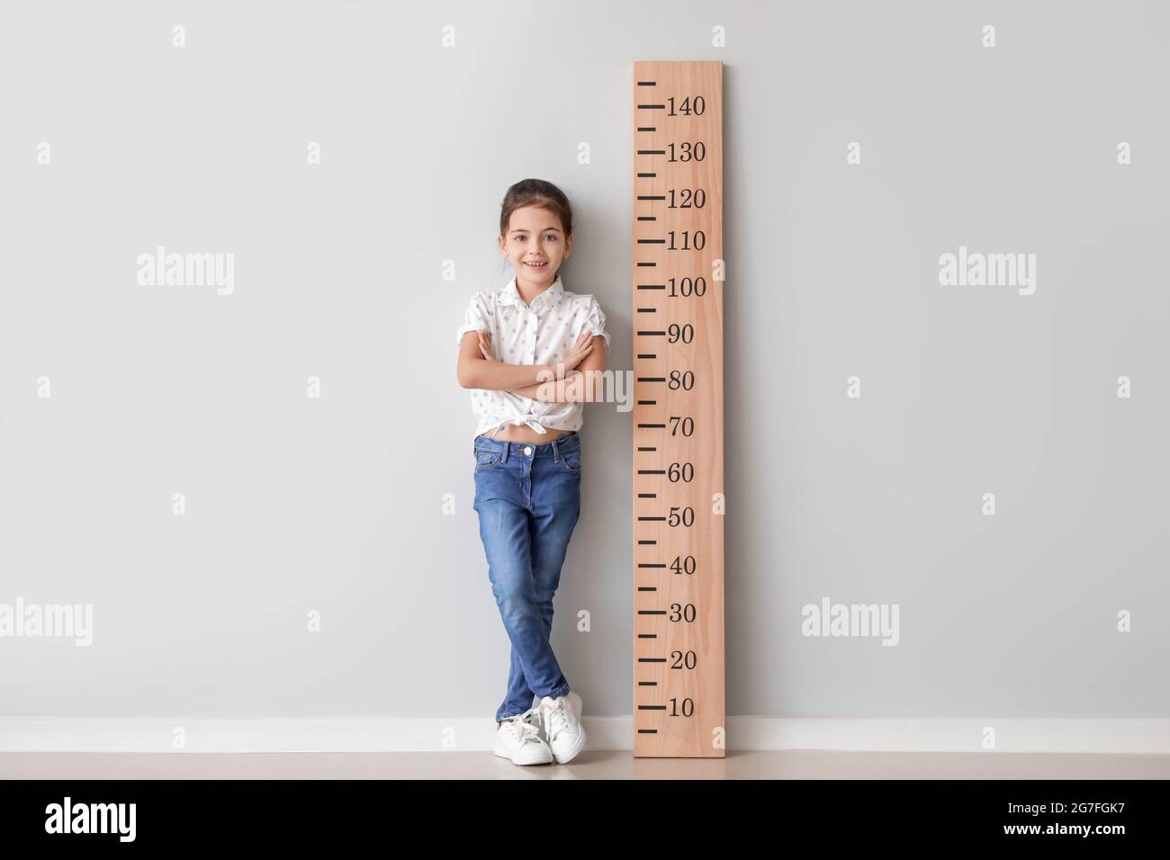 Little girl measuring height near light wall Stock Photo - Alamy