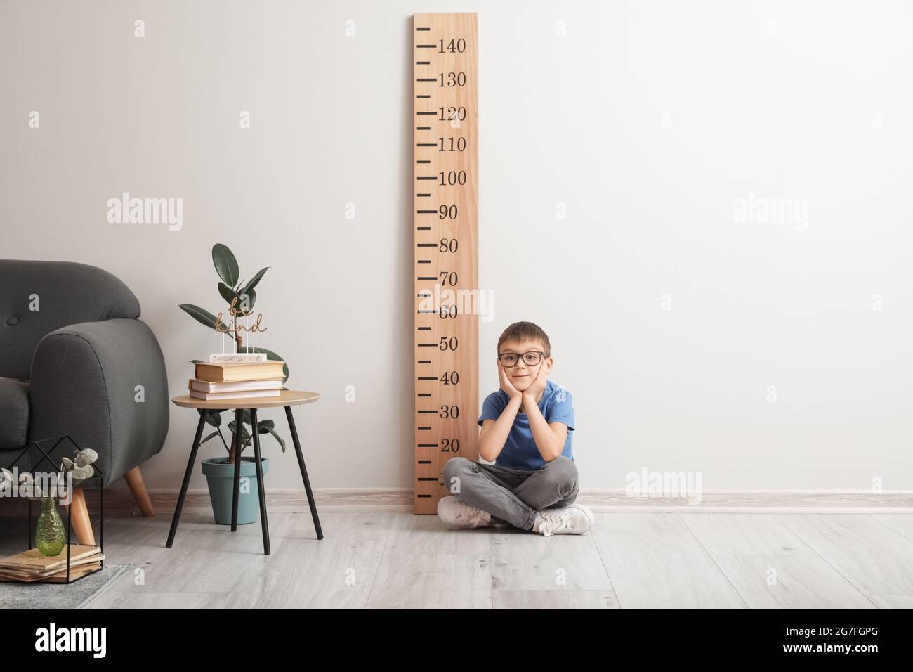 Little boy sitting near big ruler for measuring height at home Stock ...