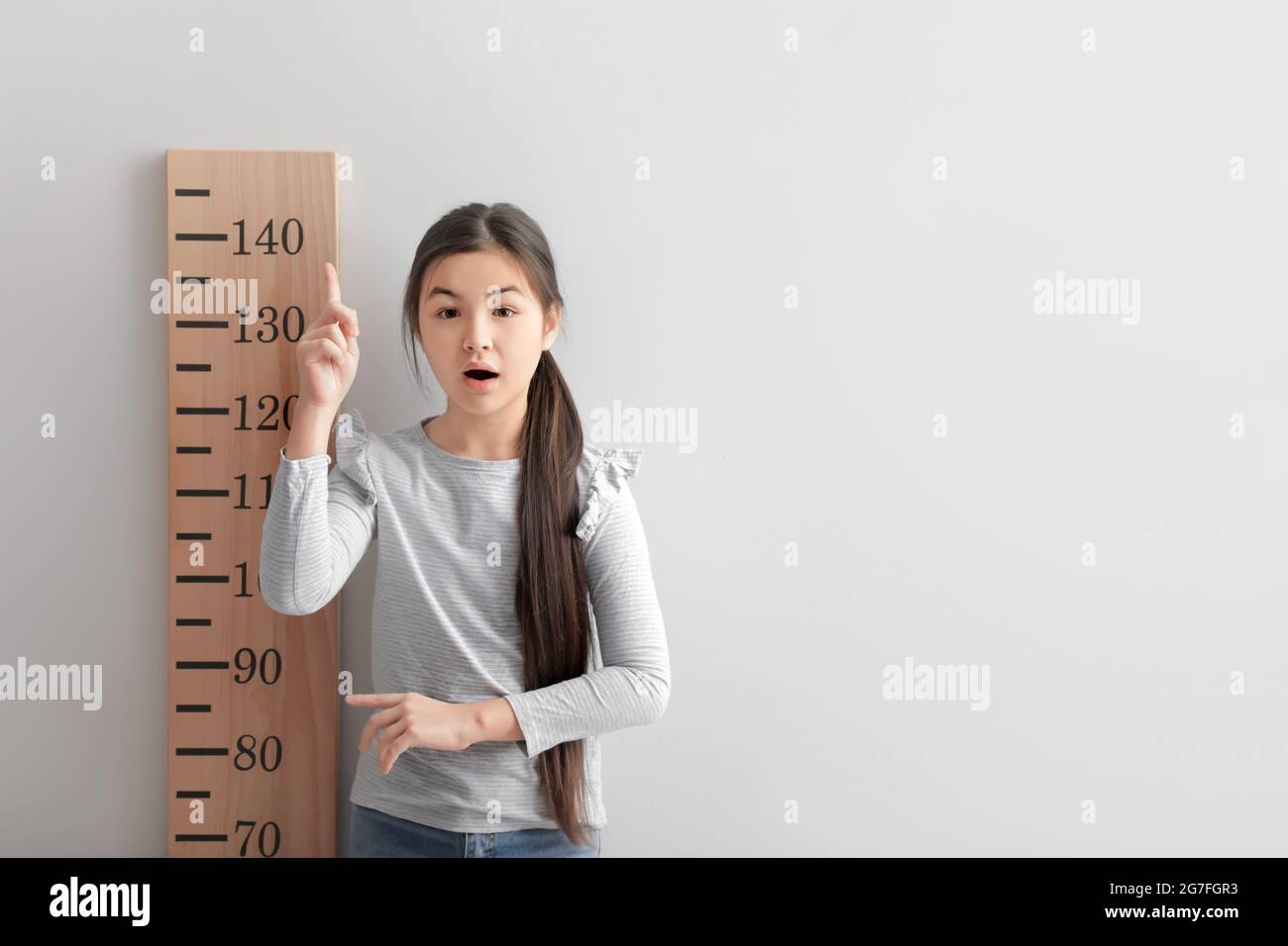 Little girl measuring height near light wall Stock Photo - Alamy