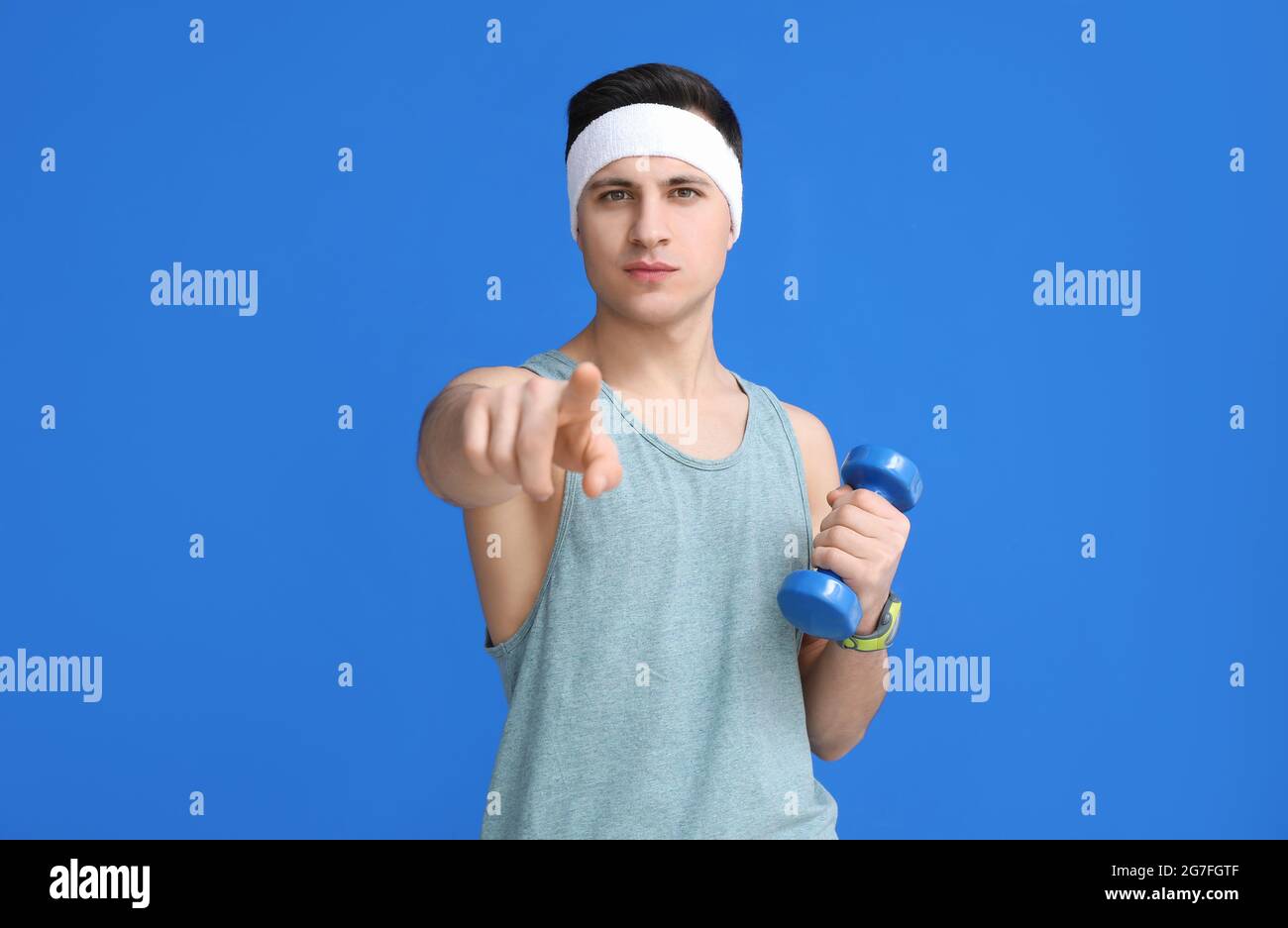 Sporty male coach with dumbbell pointing at viewer on color background ...