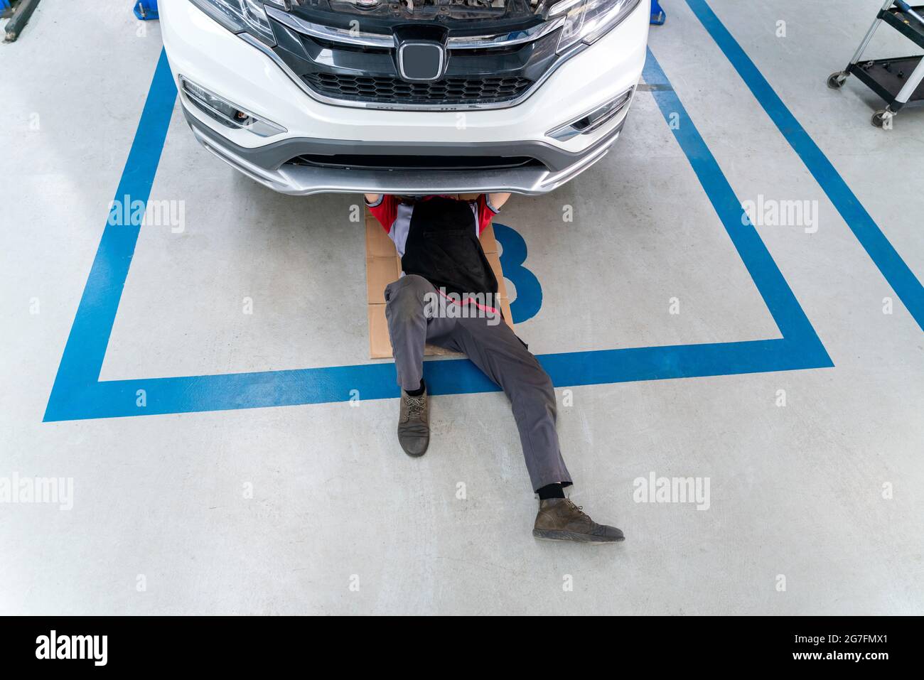 Top view of mechanic in uniform lying down and working under car, car ...