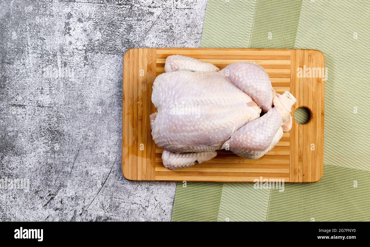 Raw chicken on a rectangular cutting wooden board on a dark grey ...