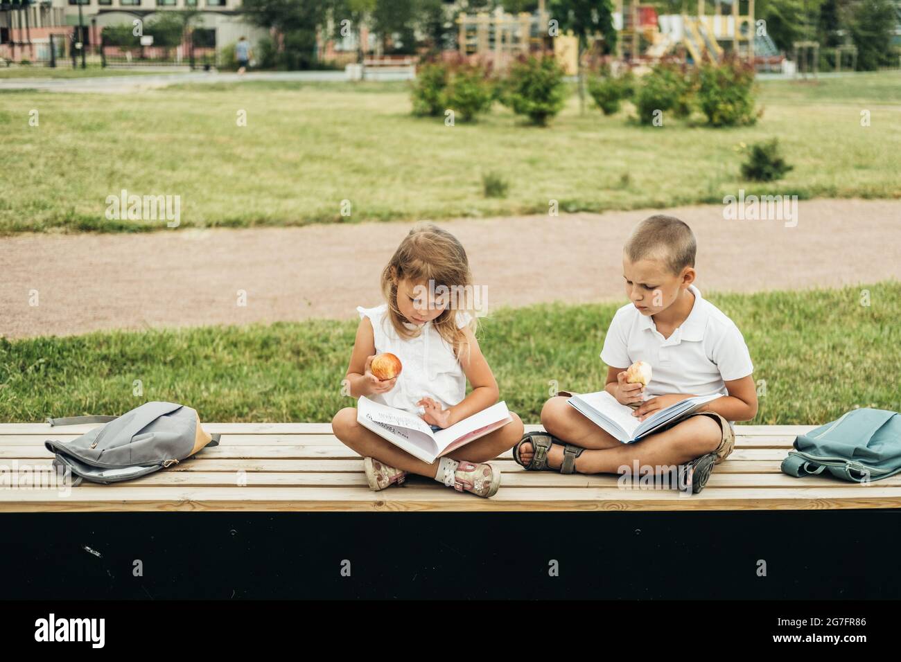 Two caucasian little students, boy and girl, eating apples during ...