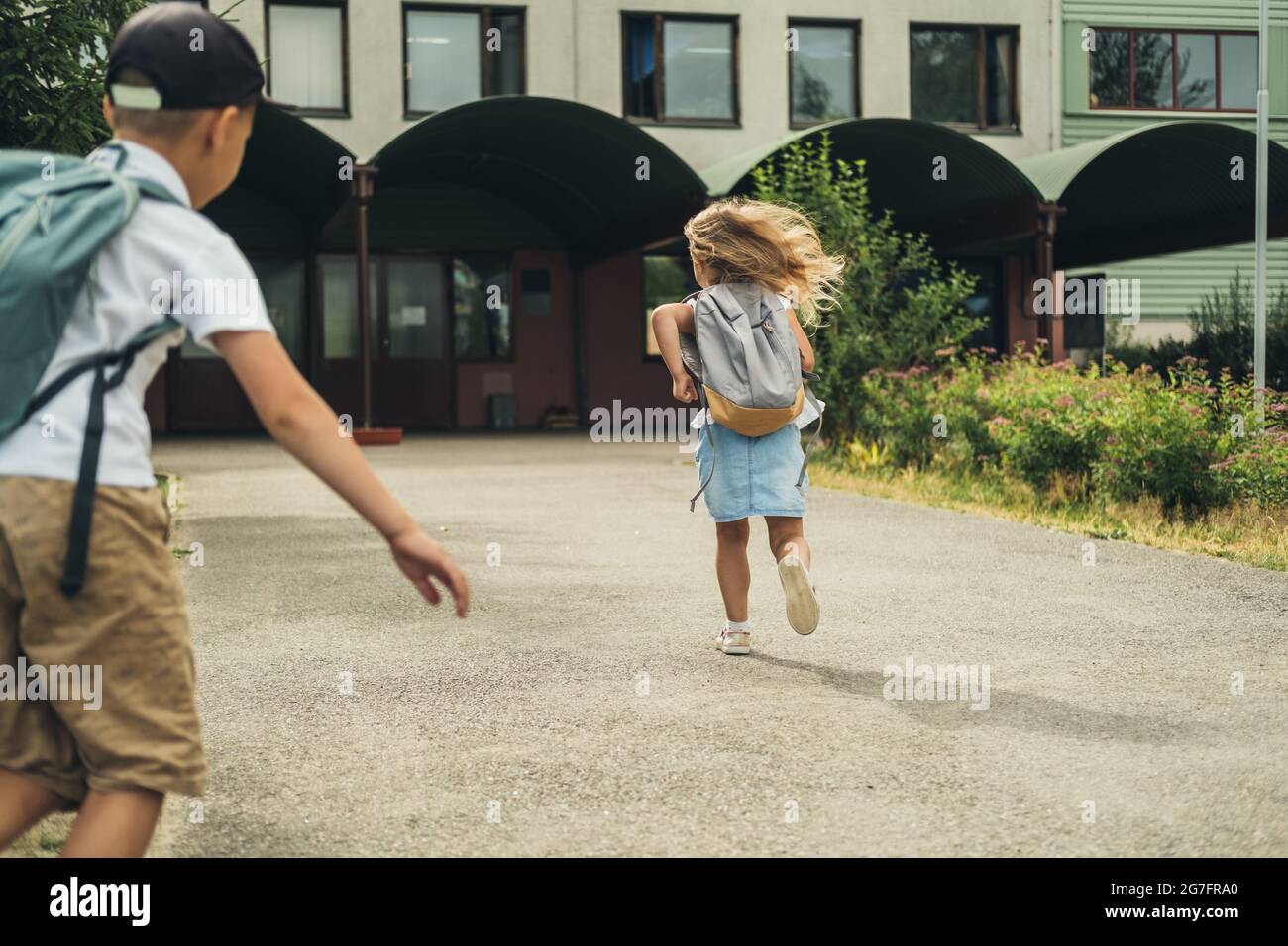 Two caucasian children, boy and girl, running to school with bags ...