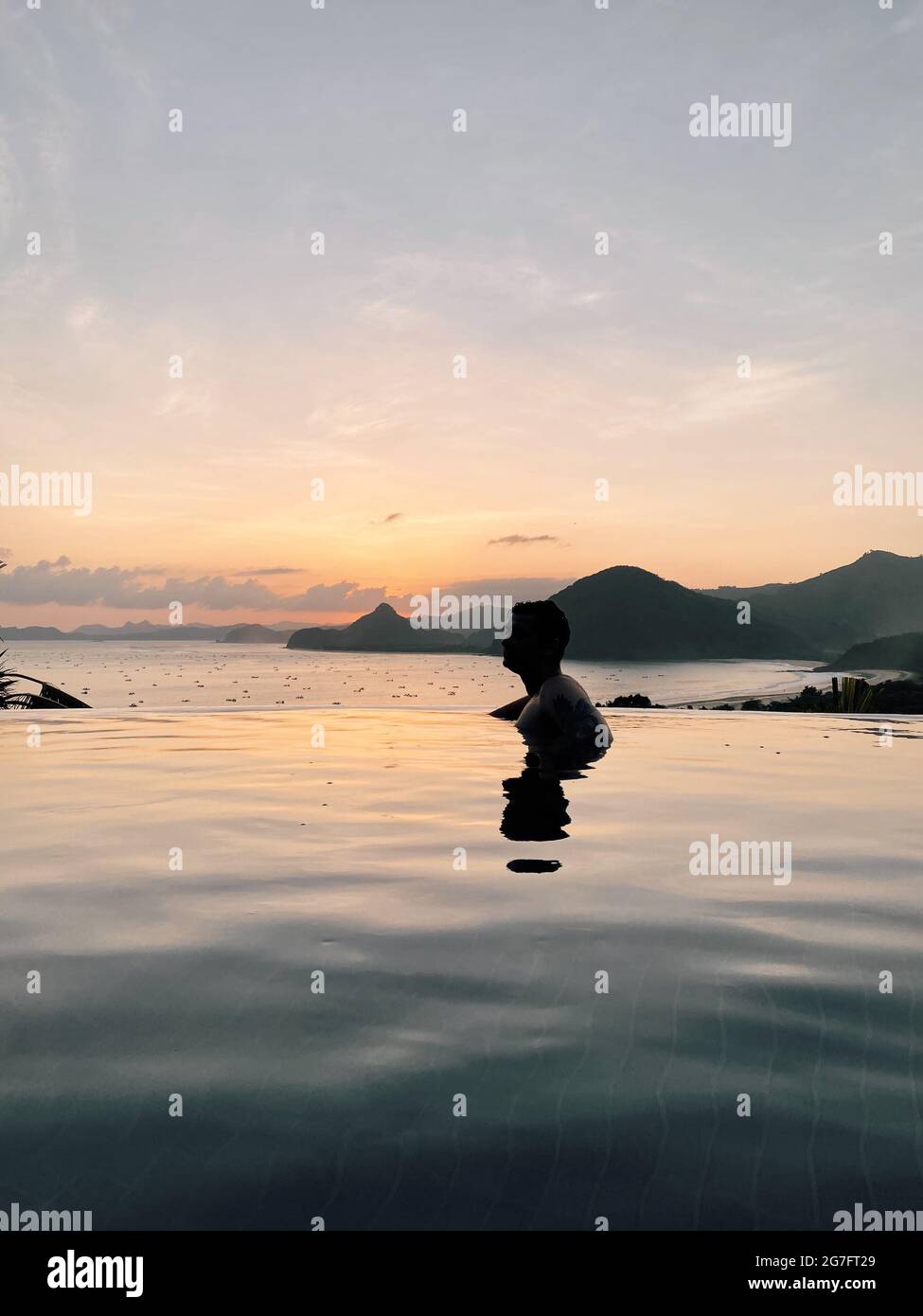 A man swimming in luxury infinity pool during sunset time Stock Photo ...