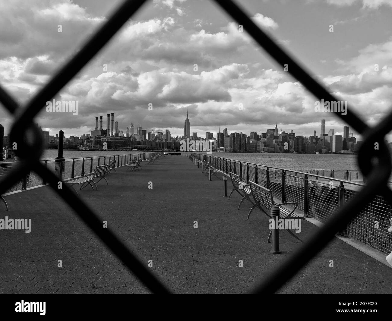 Grayscale of a trail looking at the city through the metal chain link ...