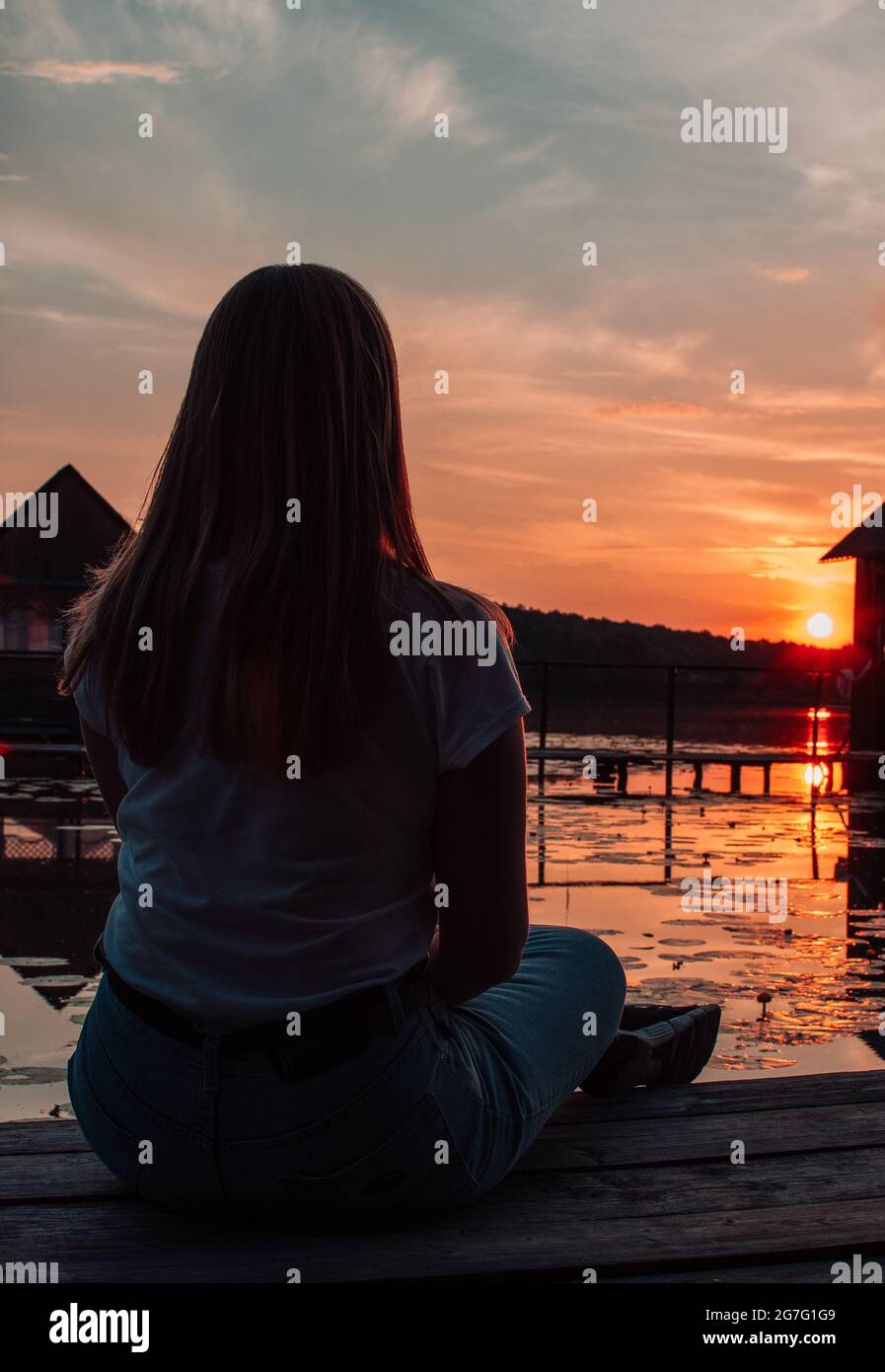 Back view of a young girl admiring the bright orange sunset while ...
