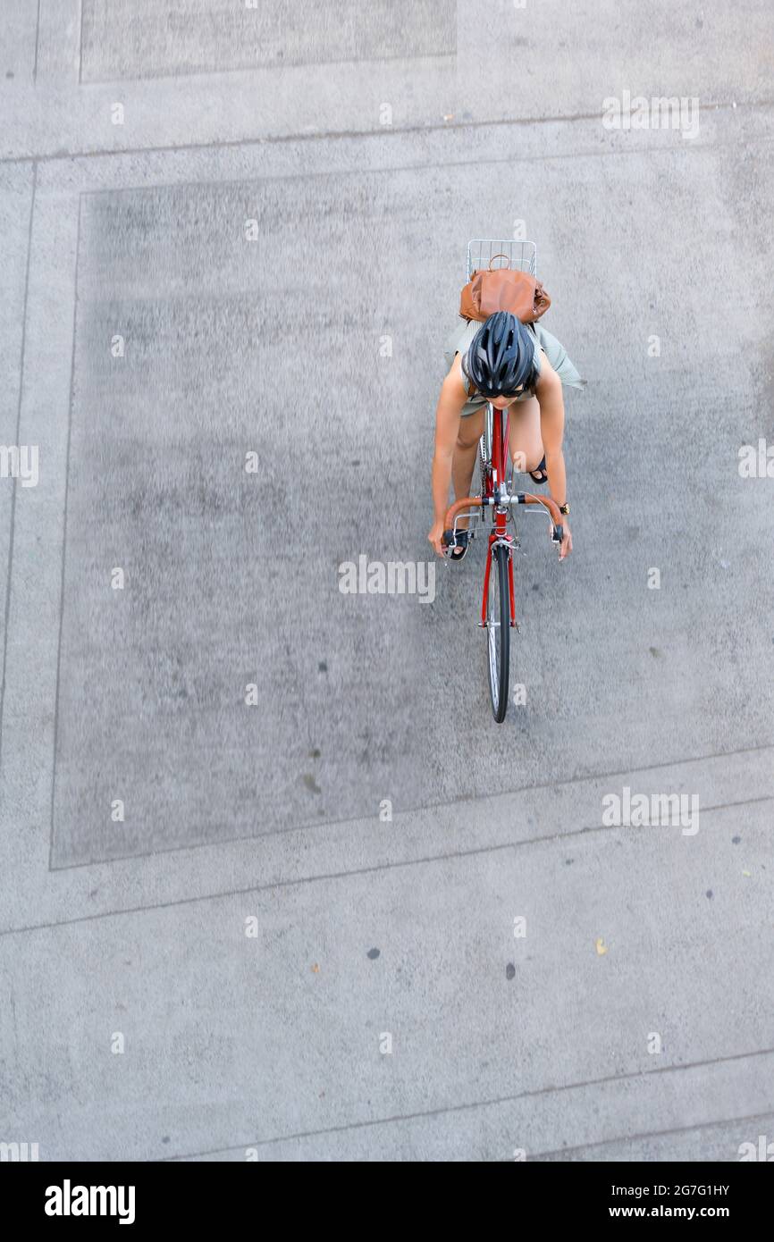 Slender girl on a bike rides a bicycle along the concrete city sidewalk ...