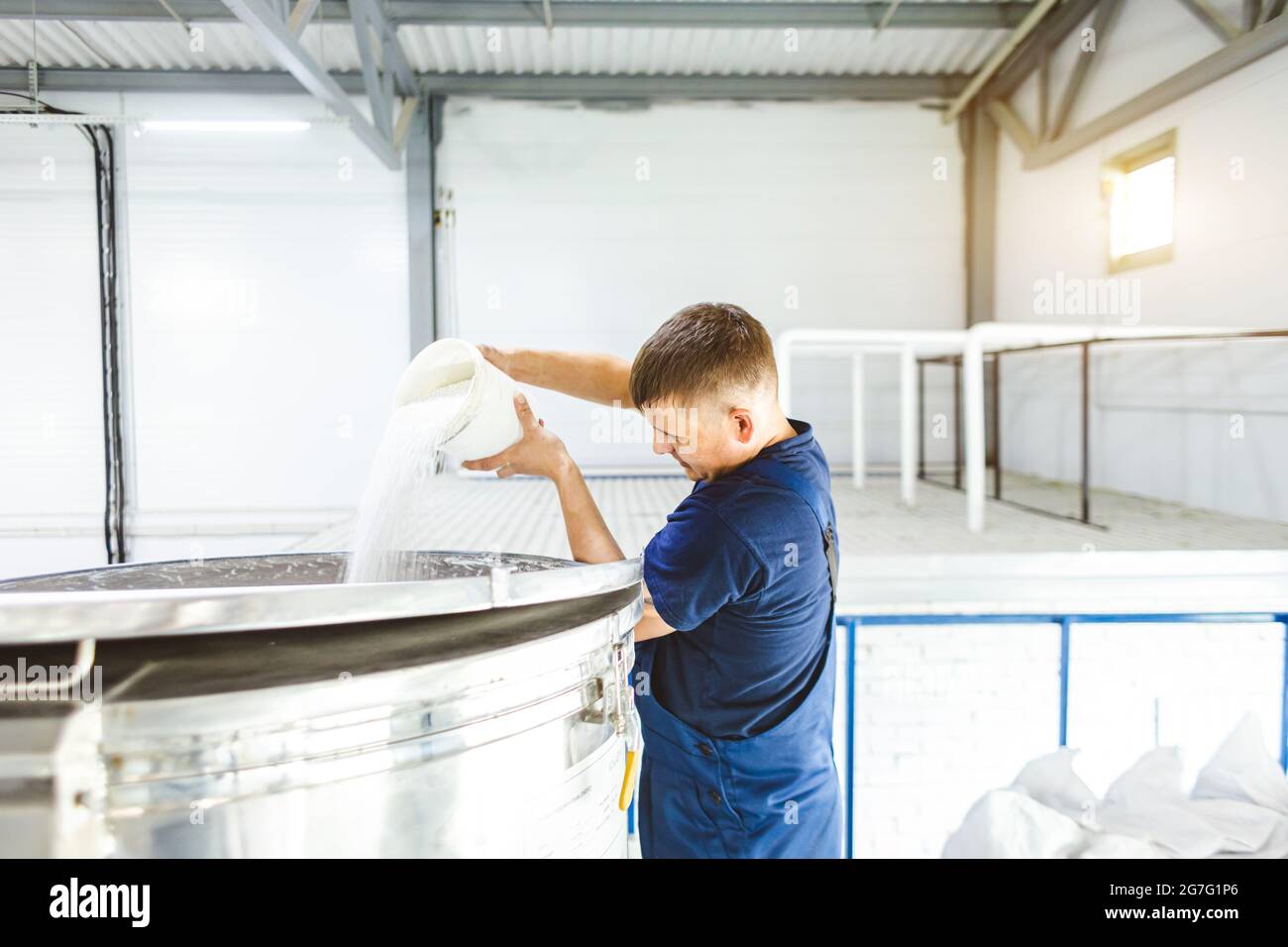 A worker in protective overalls performs a production process at an ...
