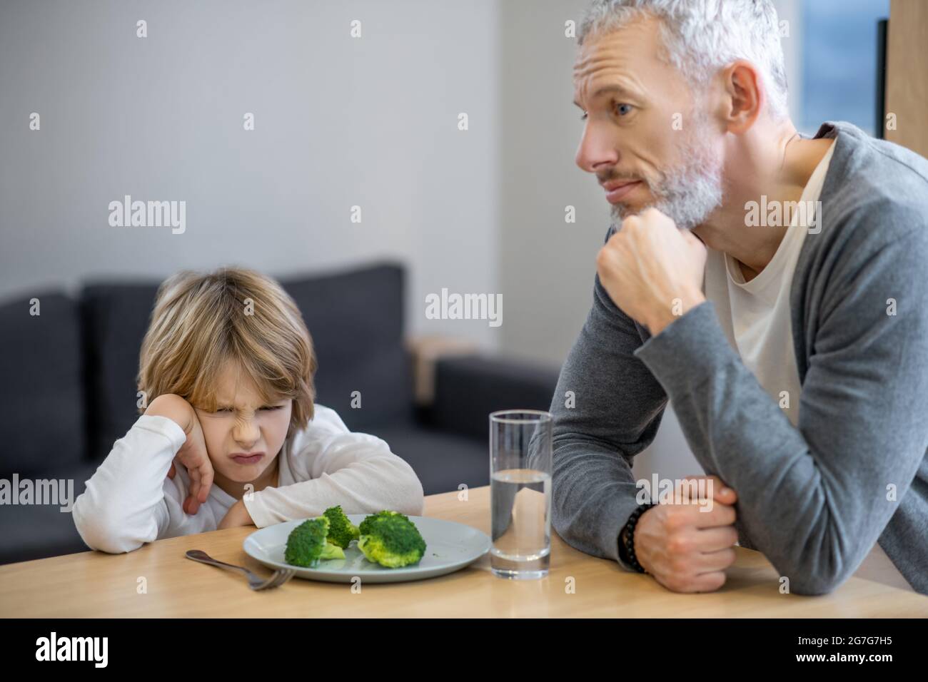 Mature man trying to make his son eat healthy while the boy looking ...