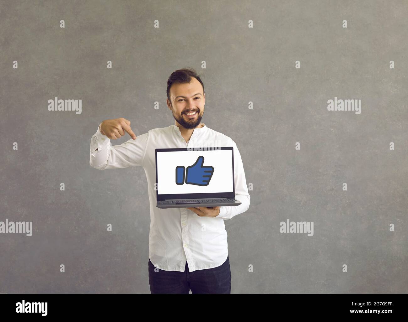 Happy young man pointing at a thumbs up symbol on the screen of his ...
