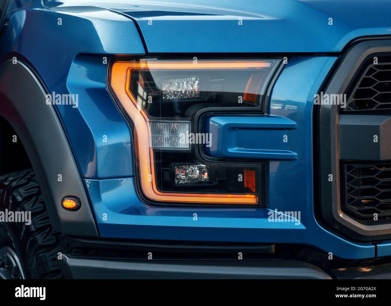 Front illuminated headlights of a blue modern SUV car. Close up detail ...