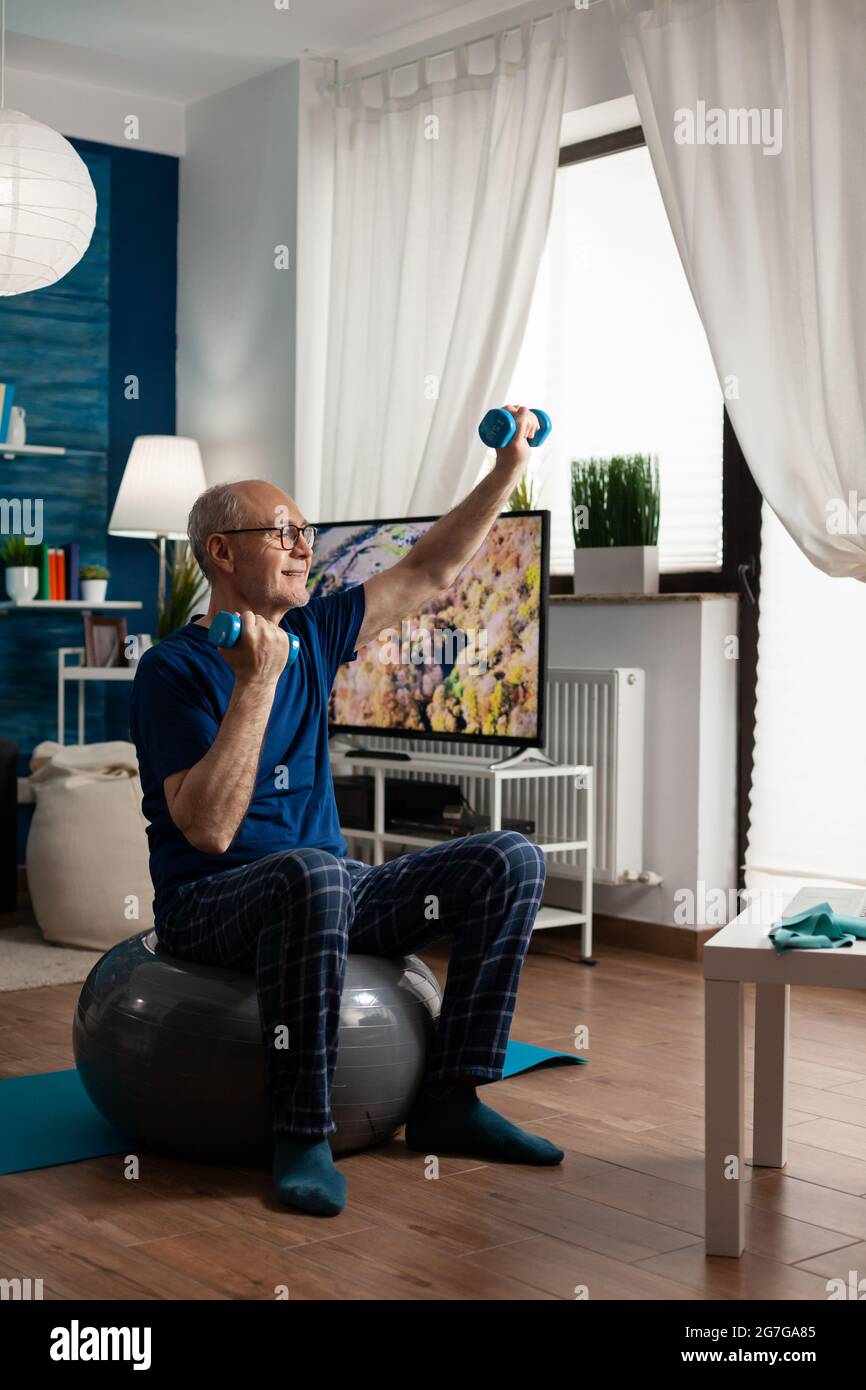 Retirement senior man sitting on aerobics swiss ball raising hand ...