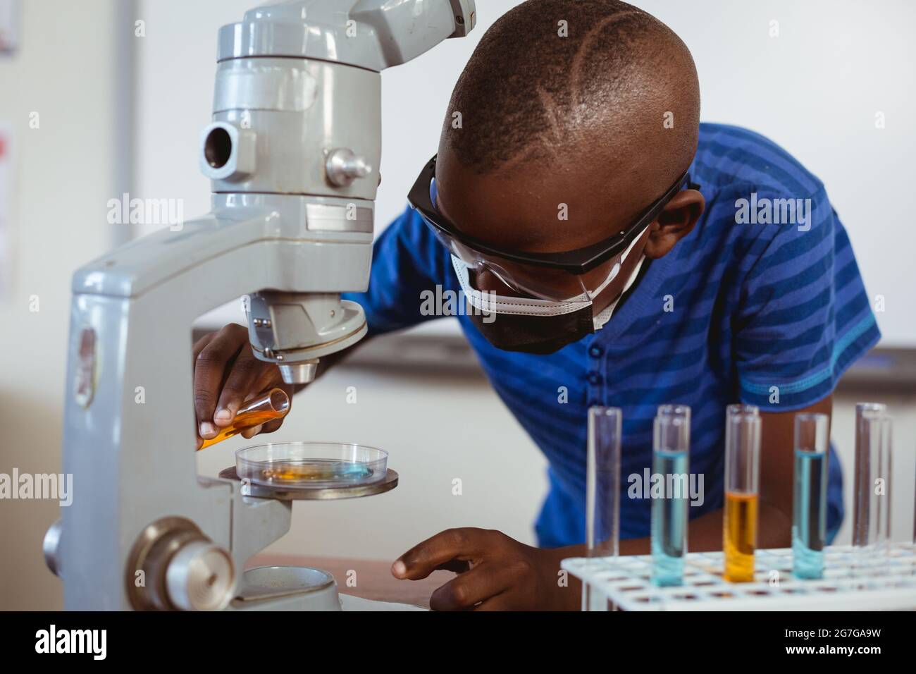 African american schoolboy in safety glasses and face mask using ...