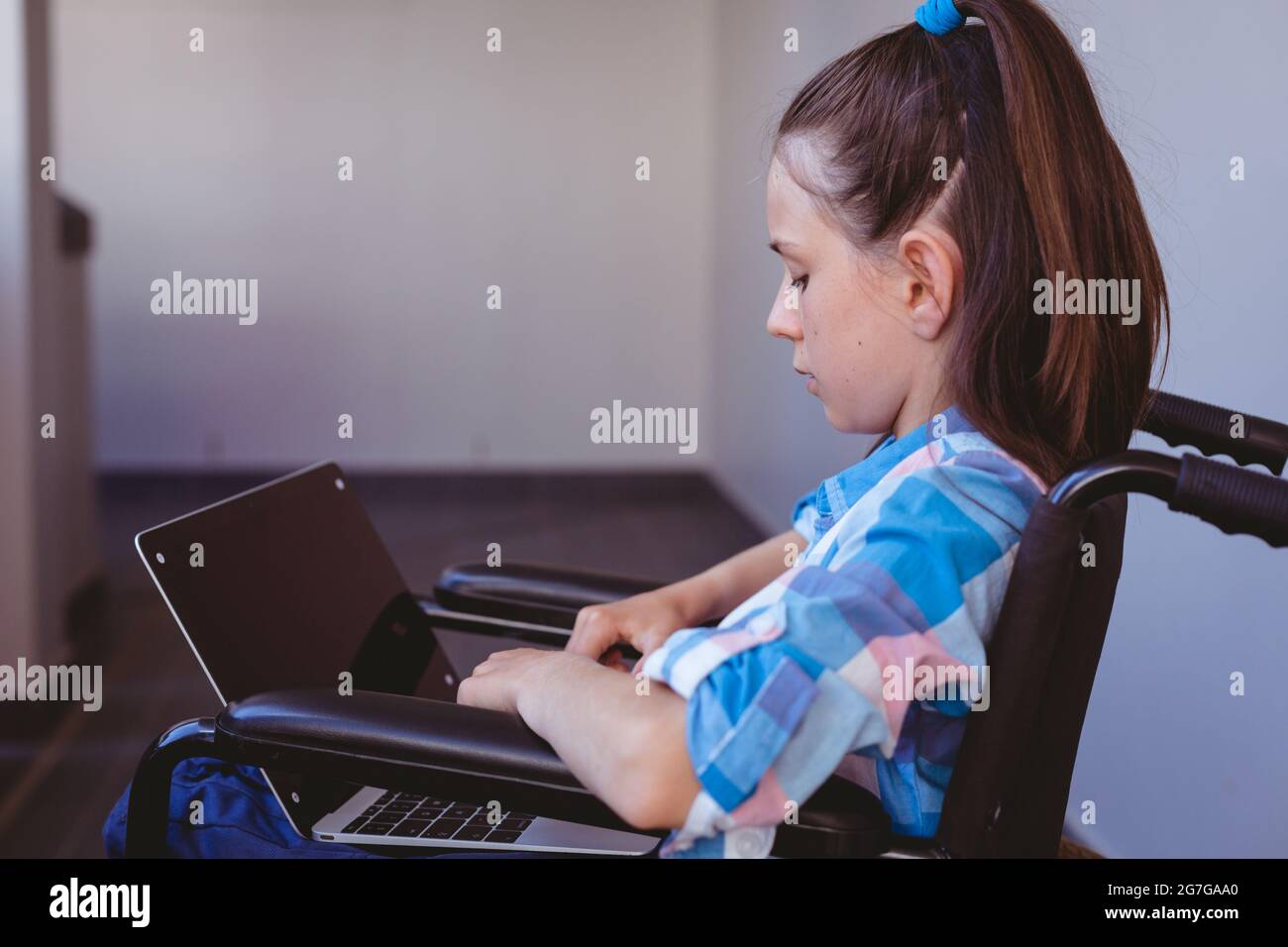 Disabled caucasian schoolgirl sitting in wheelchair using laptop in ...