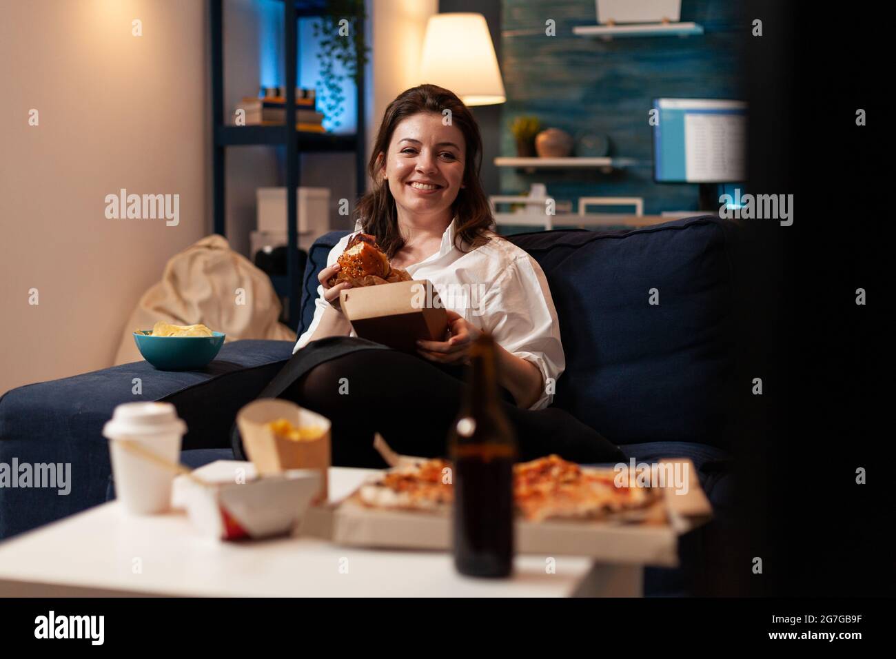 Happy woman smiling while eating tasty delicious burger watching comedy ...
