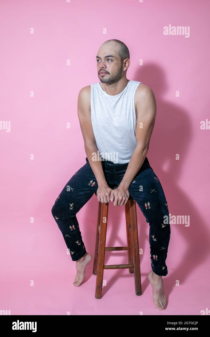 Full body shot of a young handsome bald Mexican man sitting on a chair ...