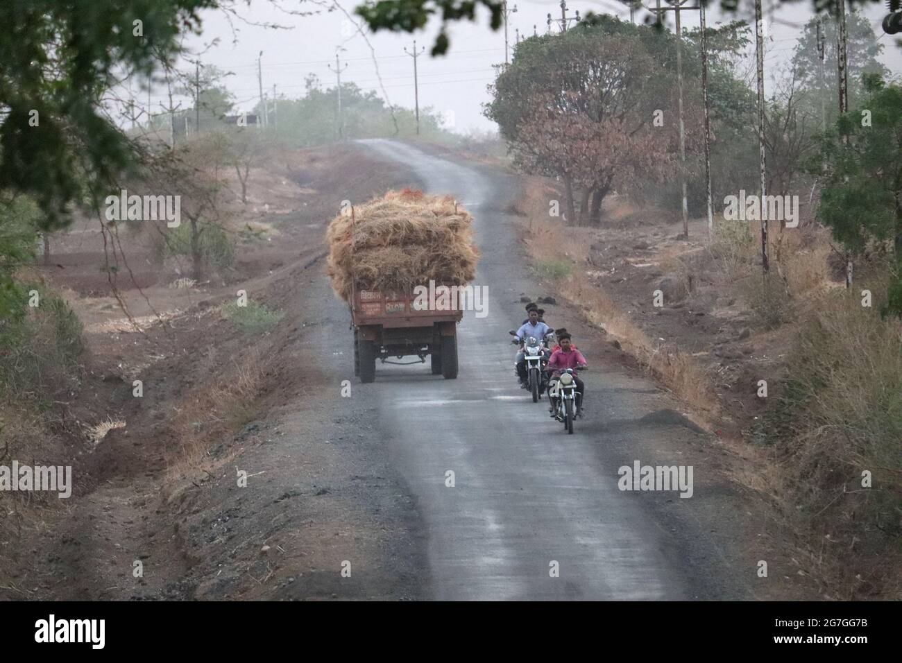Village road in rural area with tractor carrying hay or dried grass ...