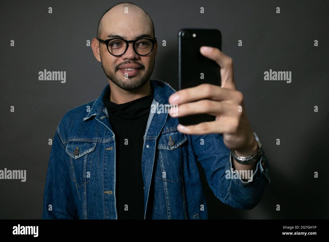 Portrait of a young handsome Mexican bald man with glasses taking a ...