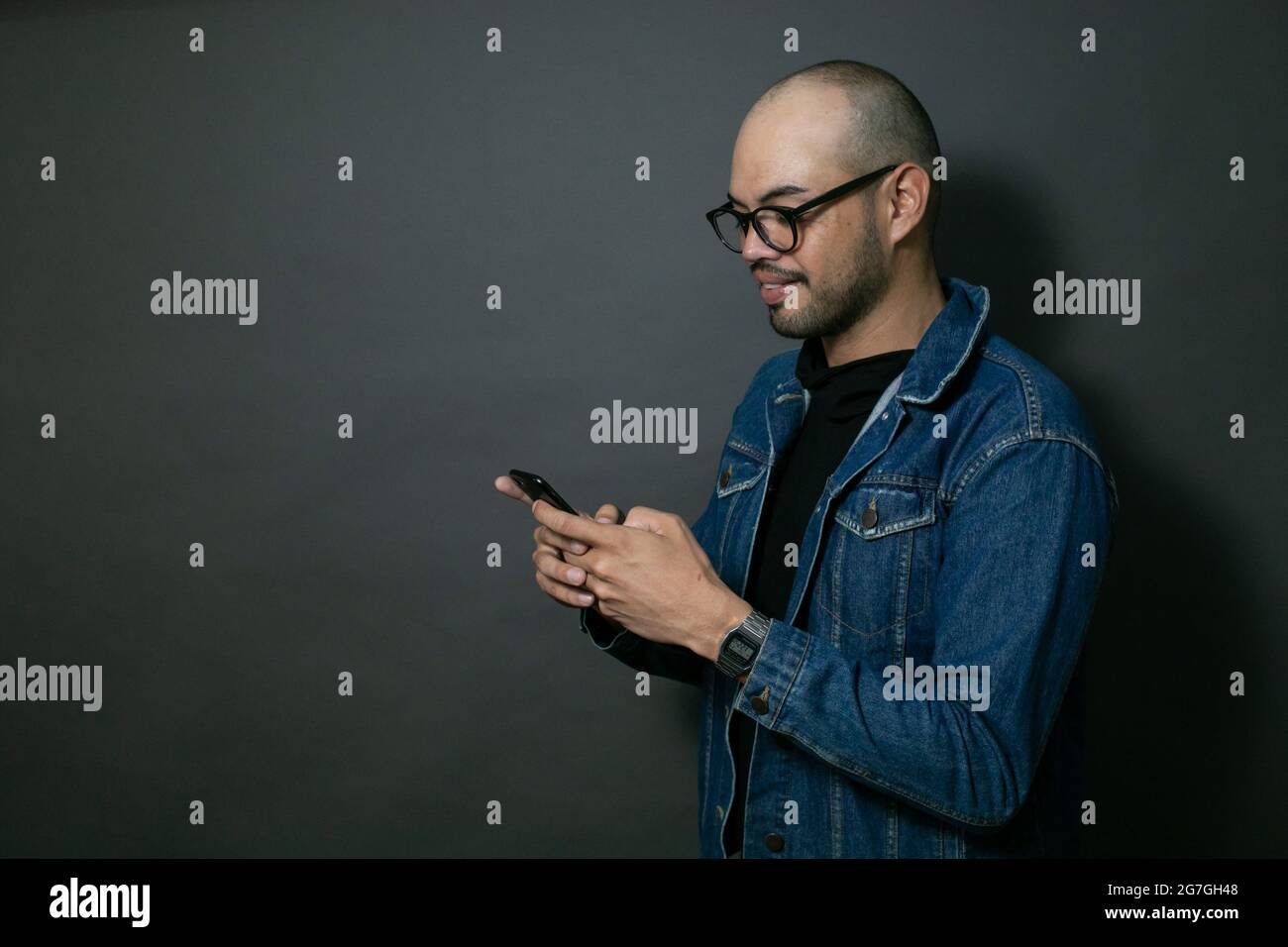 Portrait of a young handsome Mexican bald man with glasses typing on ...