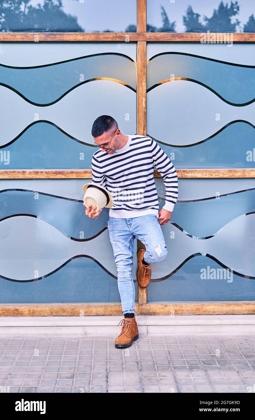 Full body adult Hispanic male in trendy outfit leaning on glass wall ...