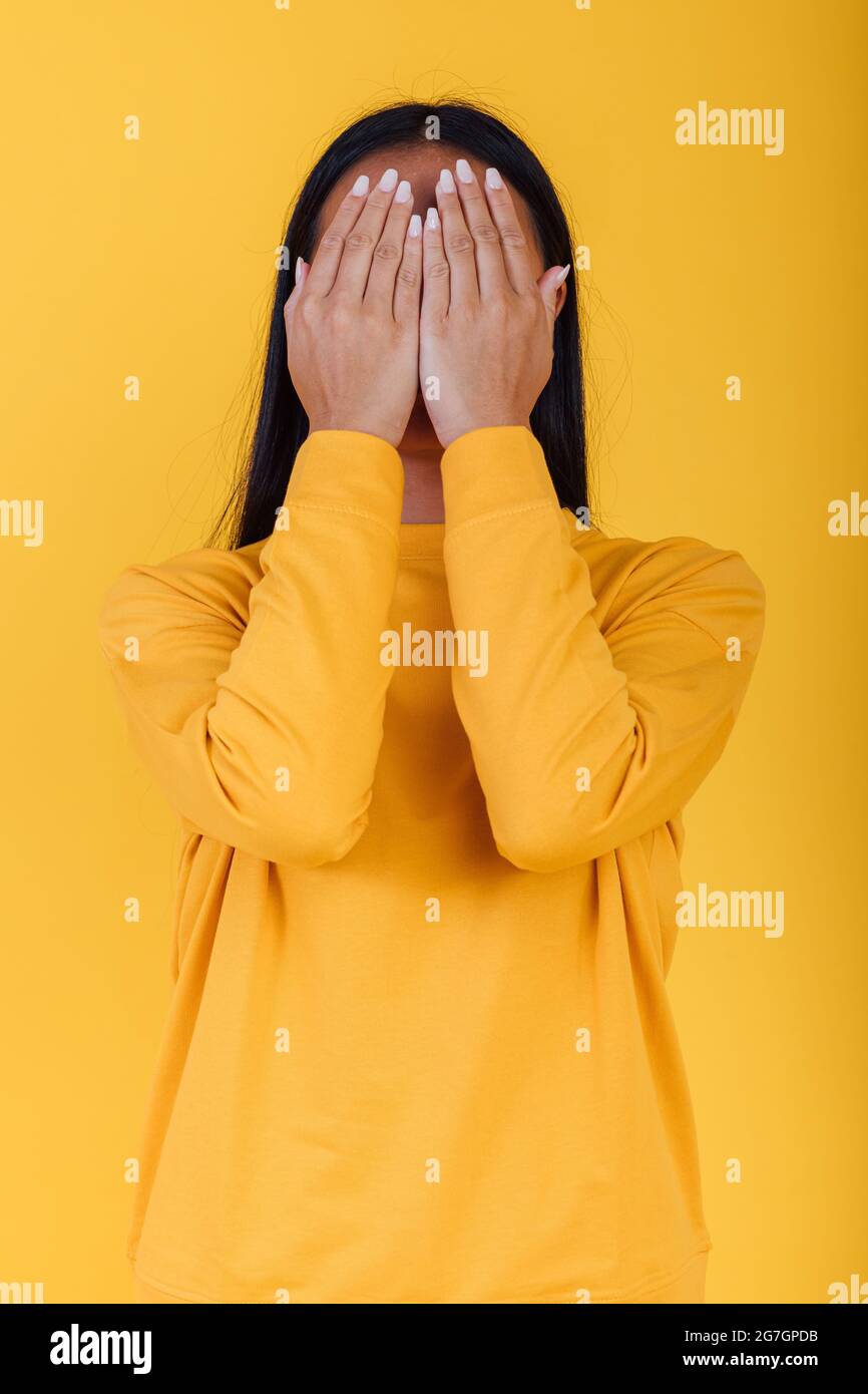 Unrecognizable female covering face with hands on bright yellow ...