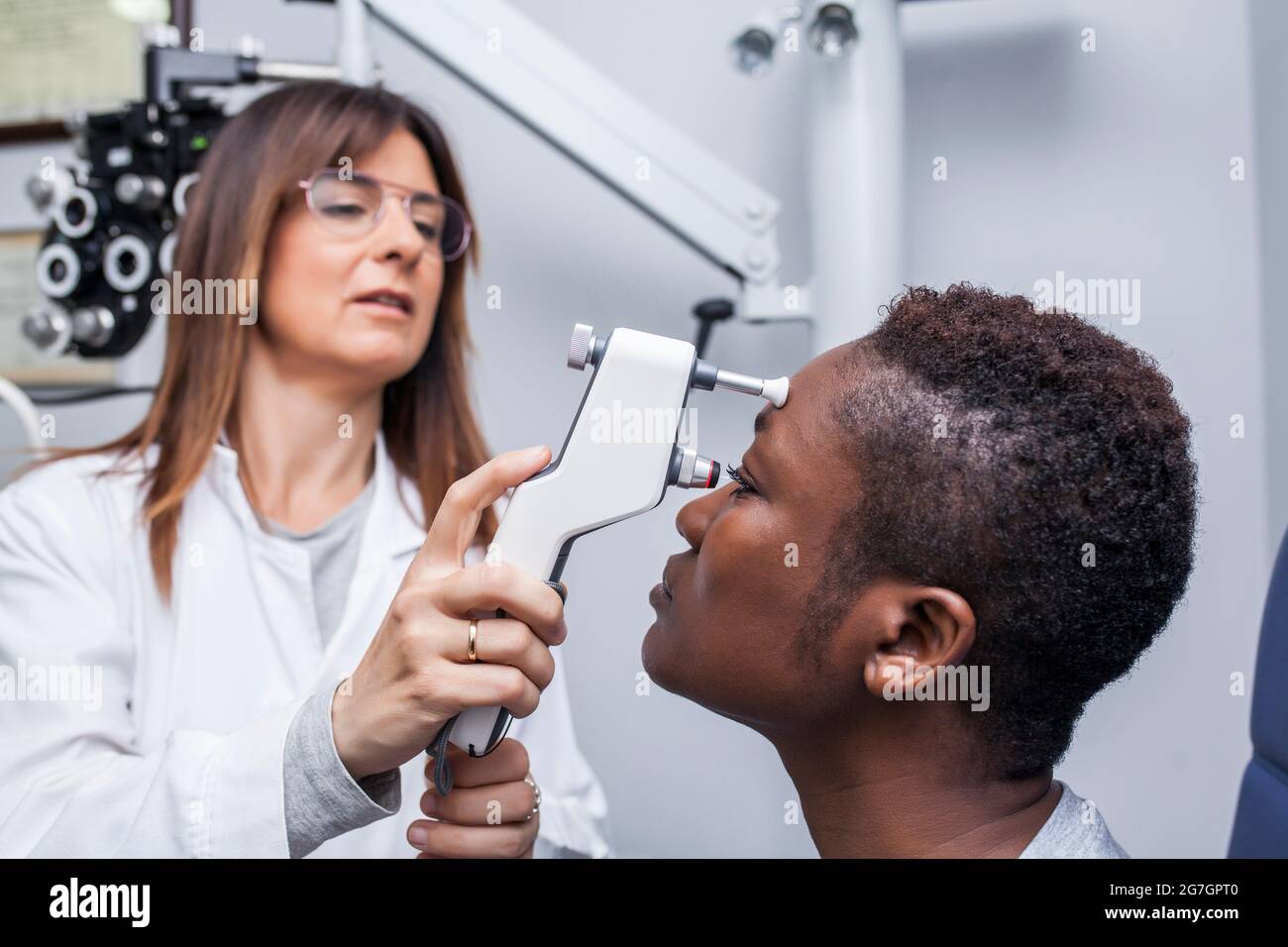 Optometrist using an ophthalmoscope during study of the eyesight of a ...