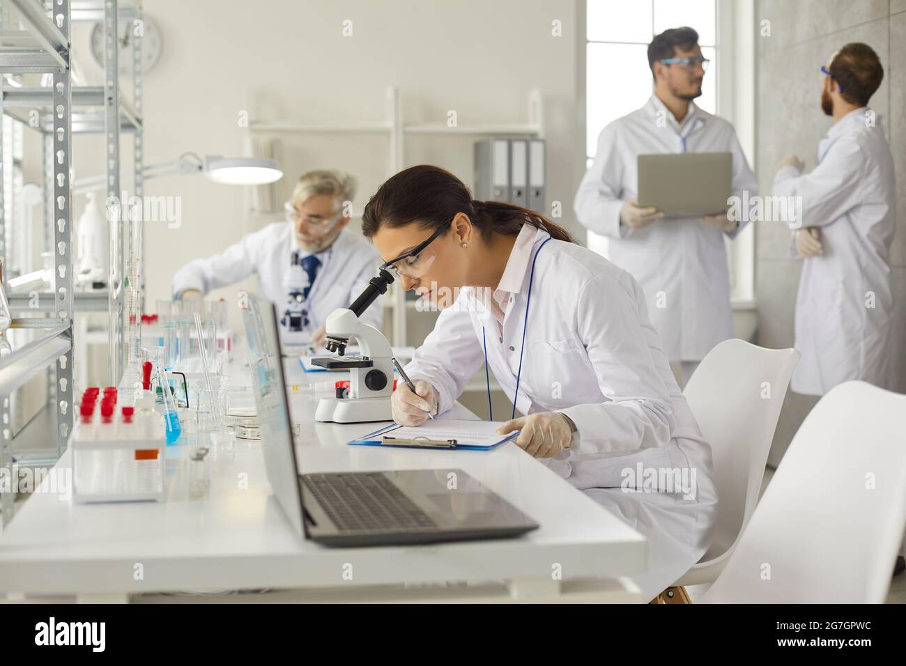 Young woman lab worker working with microscope making notes on ...