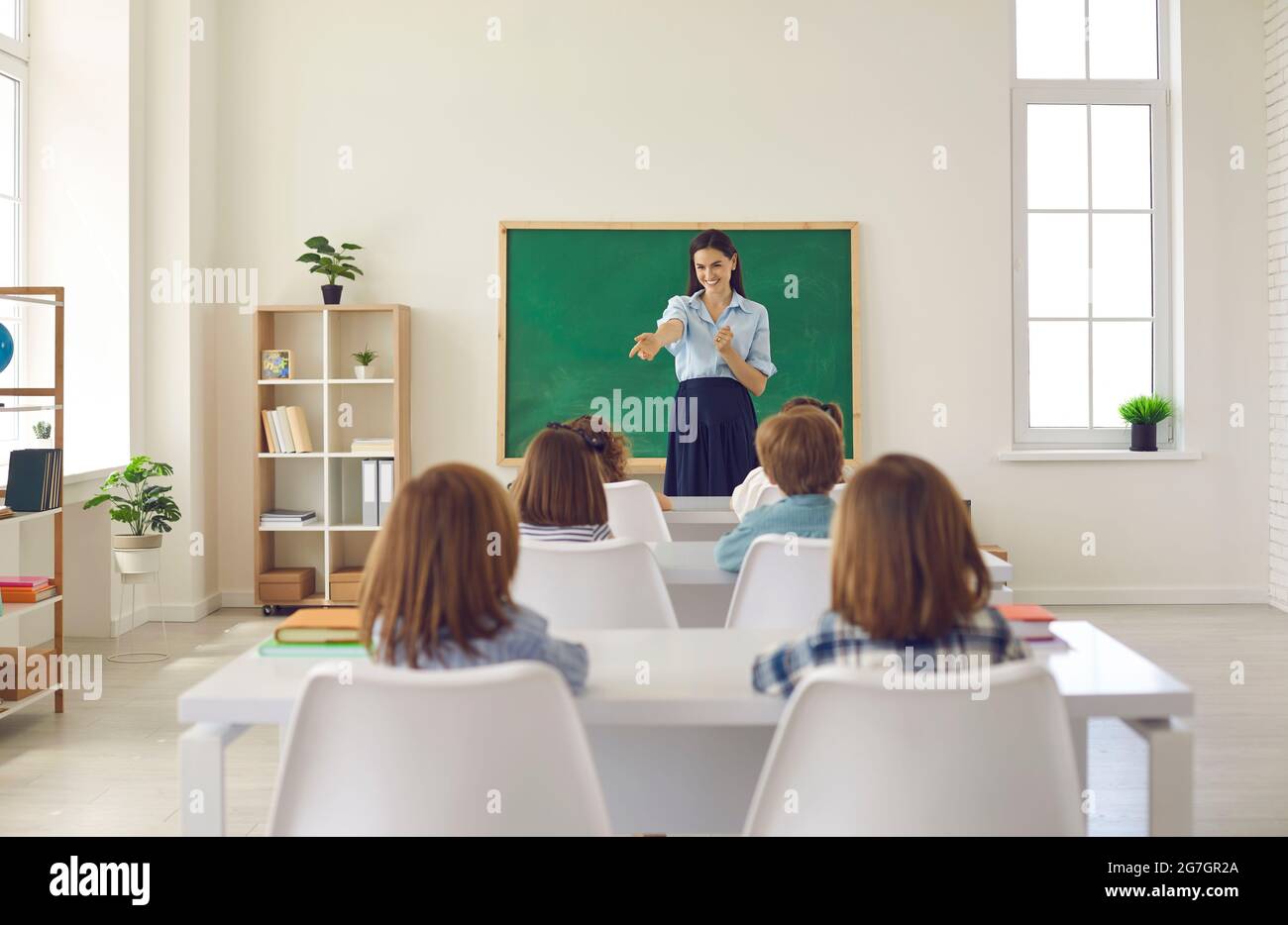 Happy smiling school teacher asks her little elementary student a ...