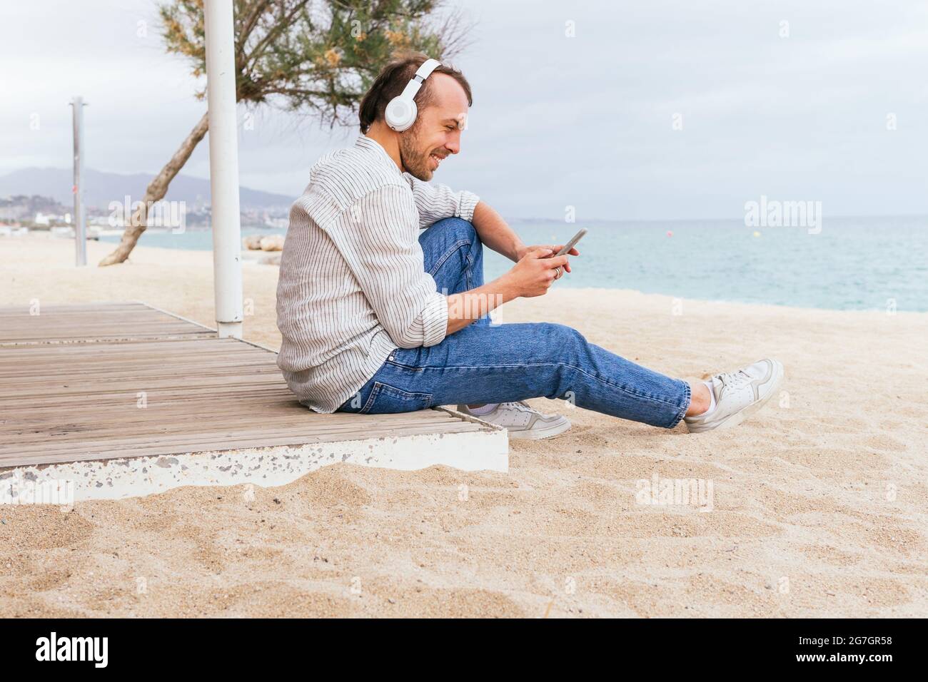 Side view of cheerful young bearded male in wireless headphones ...