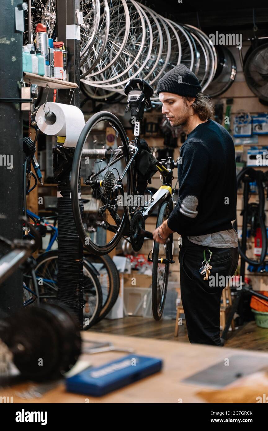 Side view of serious male mechanic repairing wheel of bicycle while ...