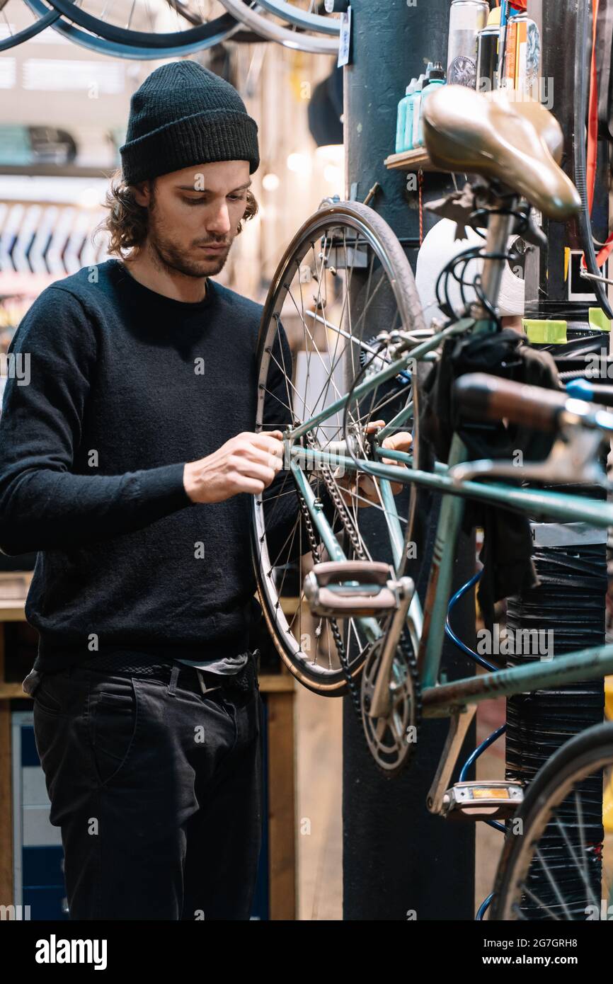 Side view of serious male mechanic repairing wheel of bicycle while ...