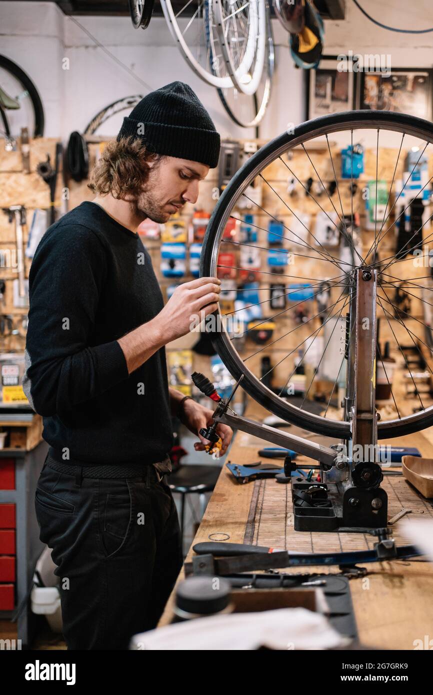 Side view of young male master examining tire on bike wheel while ...