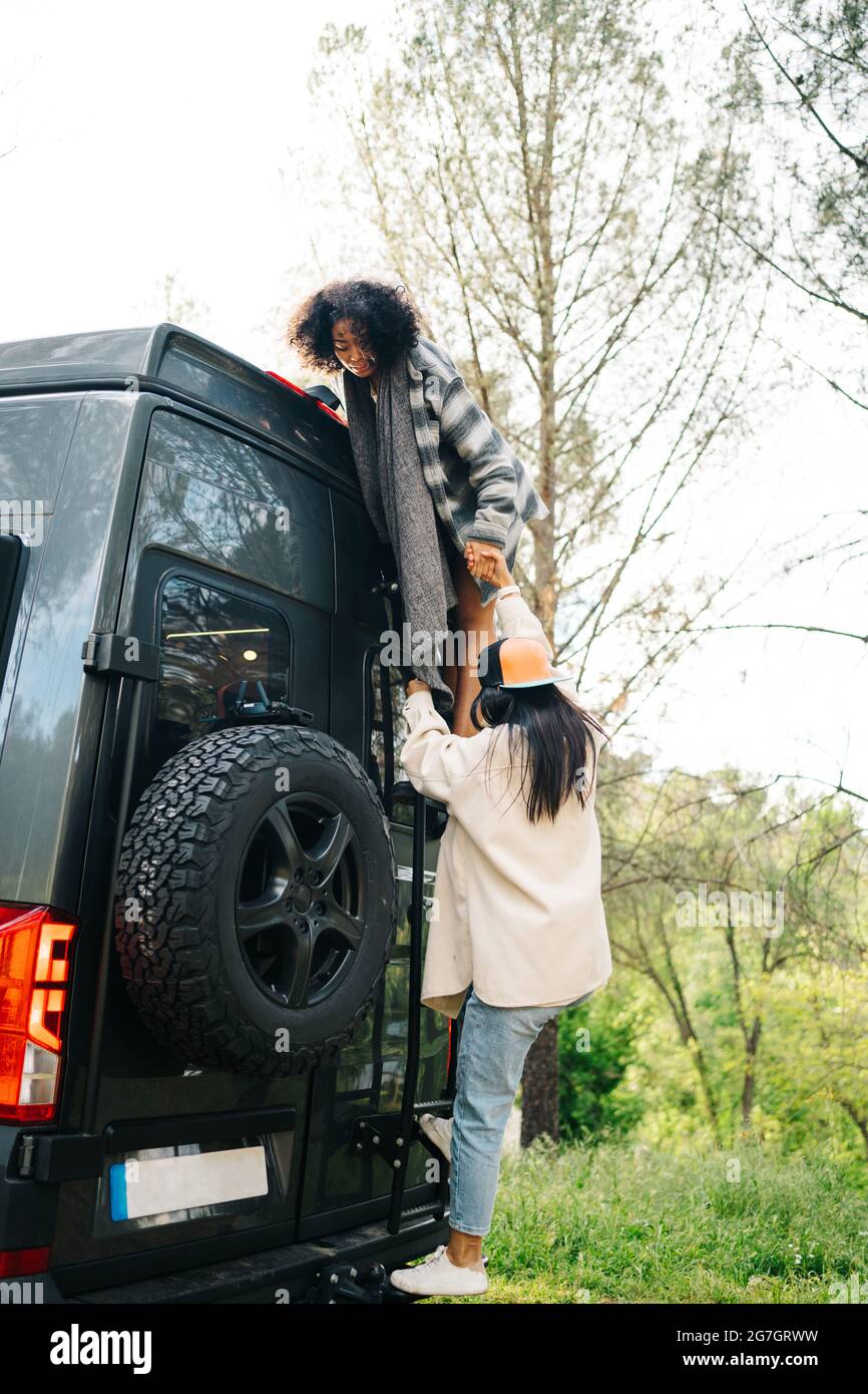 Side view of young African American Woman helping friend climbing up ...
