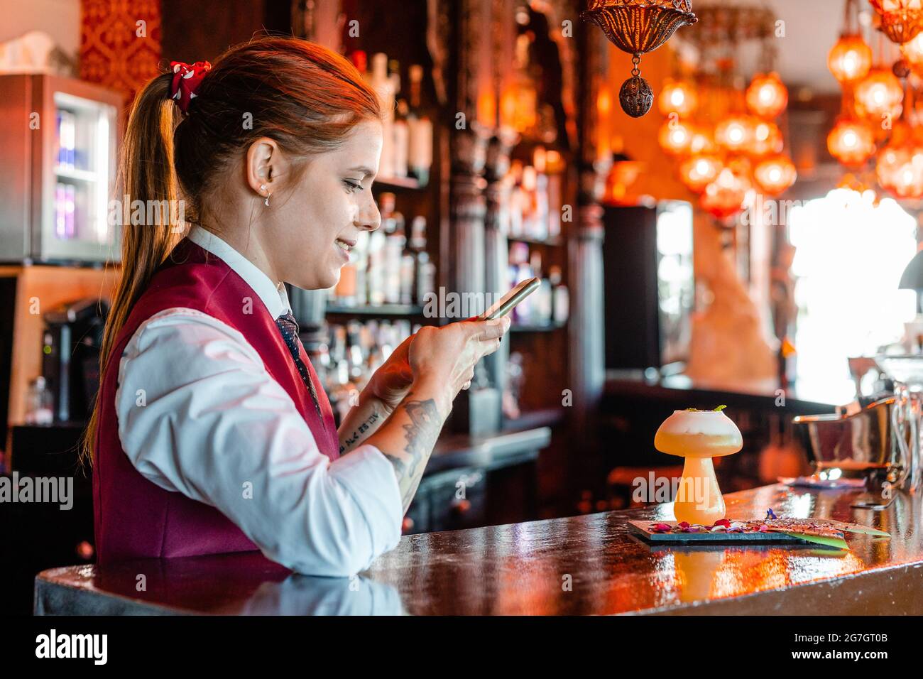 Side view of cheerful female bartender taking photo of sour cocktail in ...
