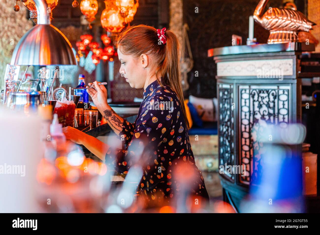 Focused female bartender garnishing fresh cocktails in glasses placed ...