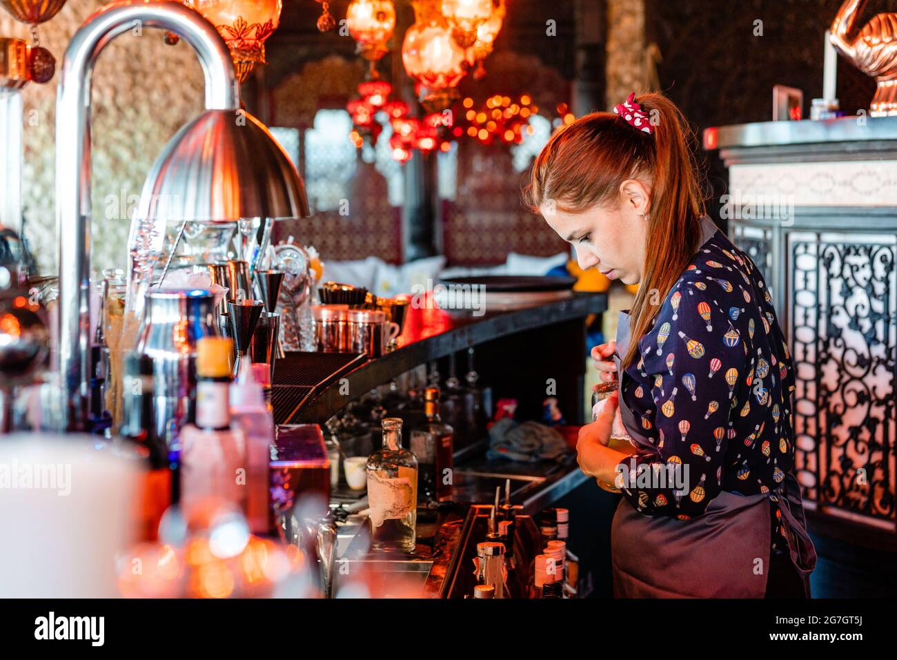 Focused female bartender garnishing fresh cocktails in glasses placed ...