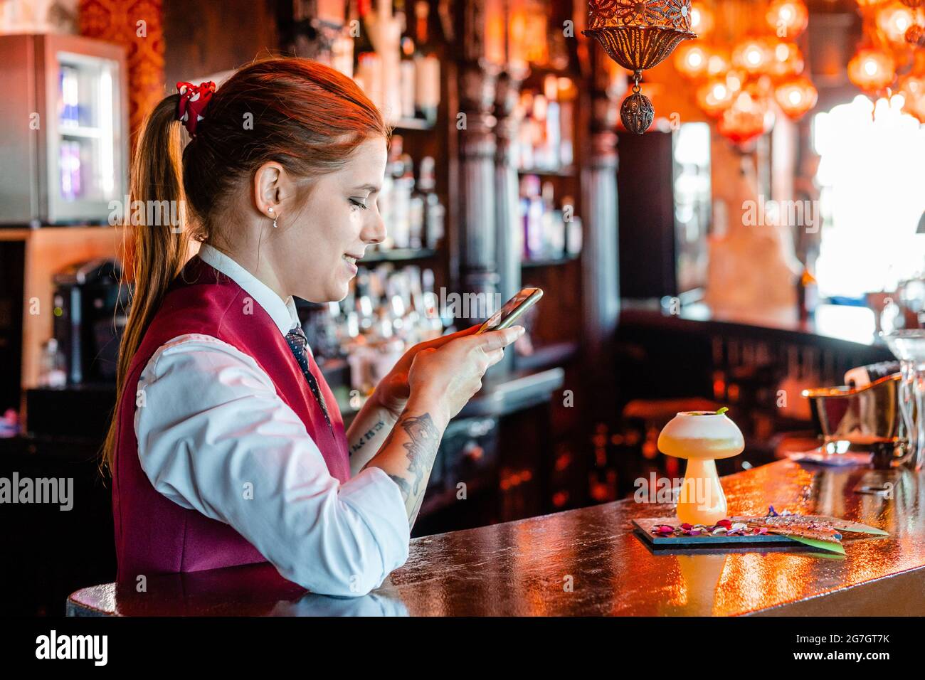 Side view of cheerful female bartender taking photo of sour cocktail in ...