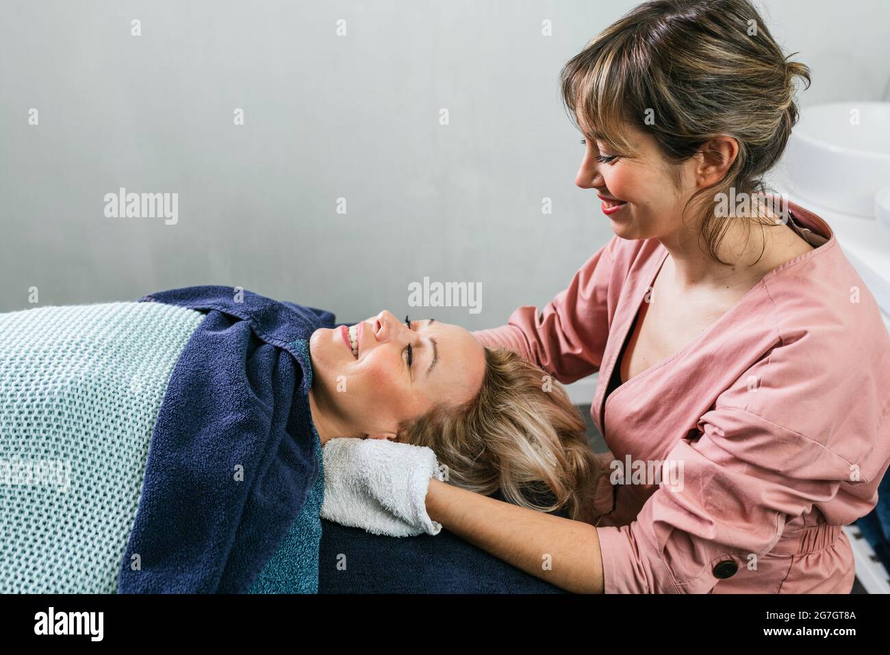 Side view of cheerful beautician wiping face of female client with ...