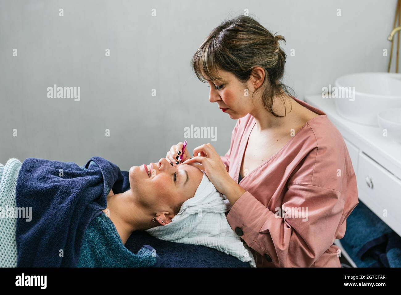 Side view of female cosmetologist plucking eyebrows on face of Woman ...
