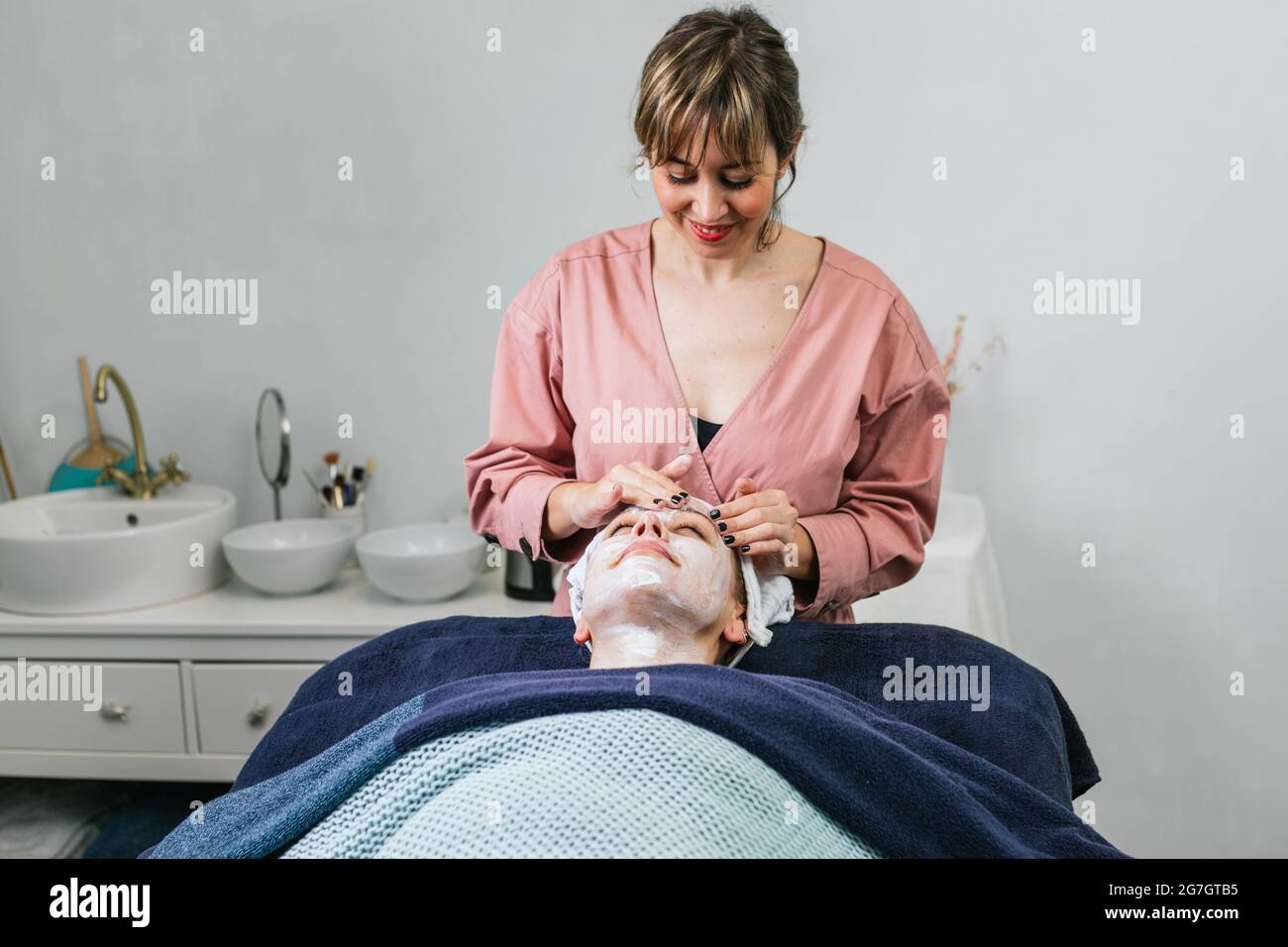 Female cosmetician applying facial cleanser on face of female client ...