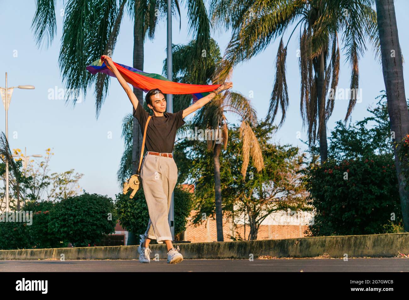 Content gay male walking with rainbow LGBT flag in raised hands along ...