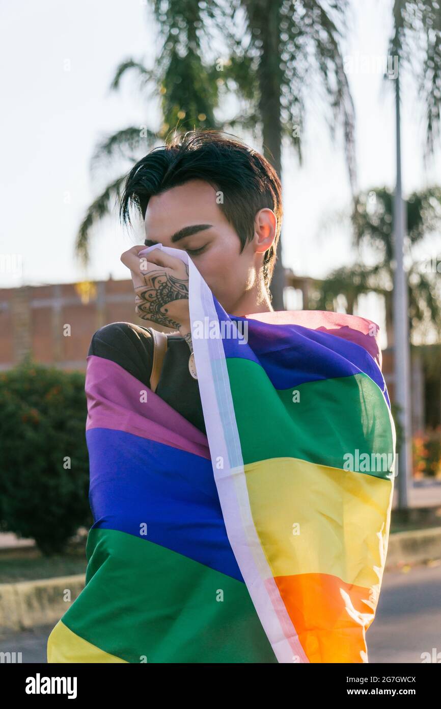 Tranquil gay male with closed eyes wrapped in colorful LGBT flag in ...