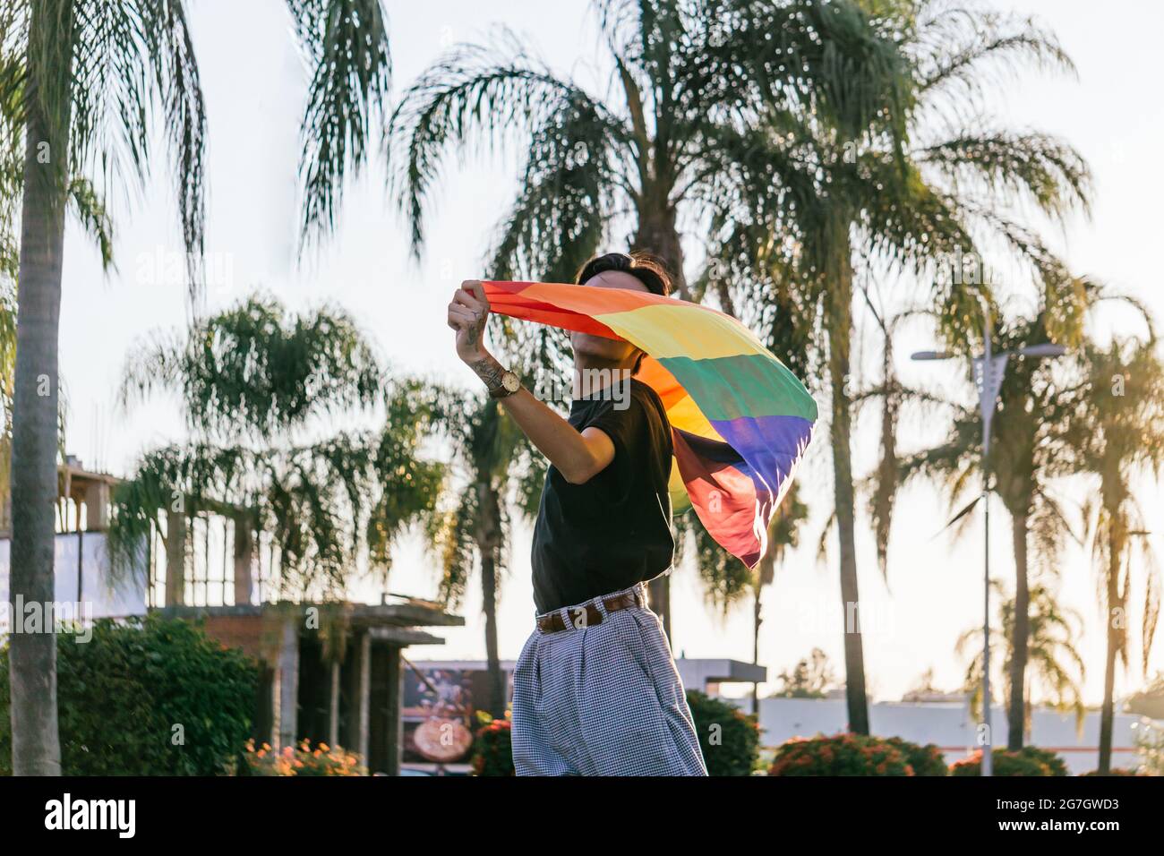 Delighted male gay standing with eyes closed raising rainbow LGBT flag ...