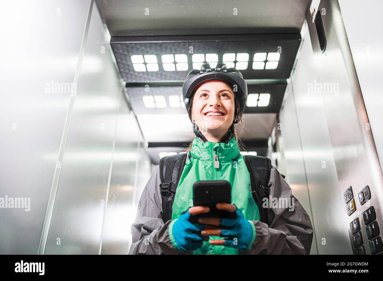 Low angle of glad female courier in uniform and helmet smiling and ...