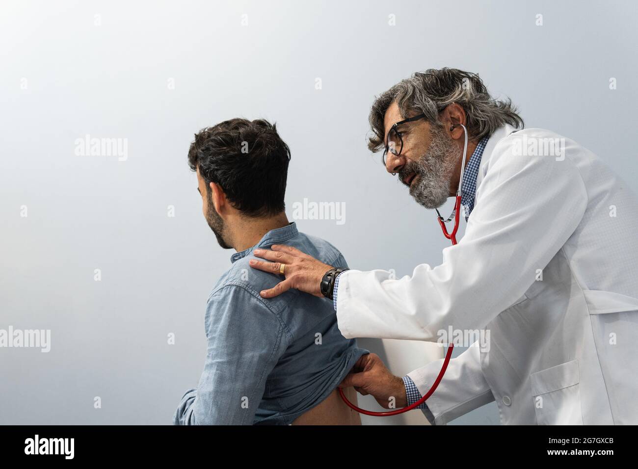 Side view of elderly male doctor examining patient with stethoscope ...