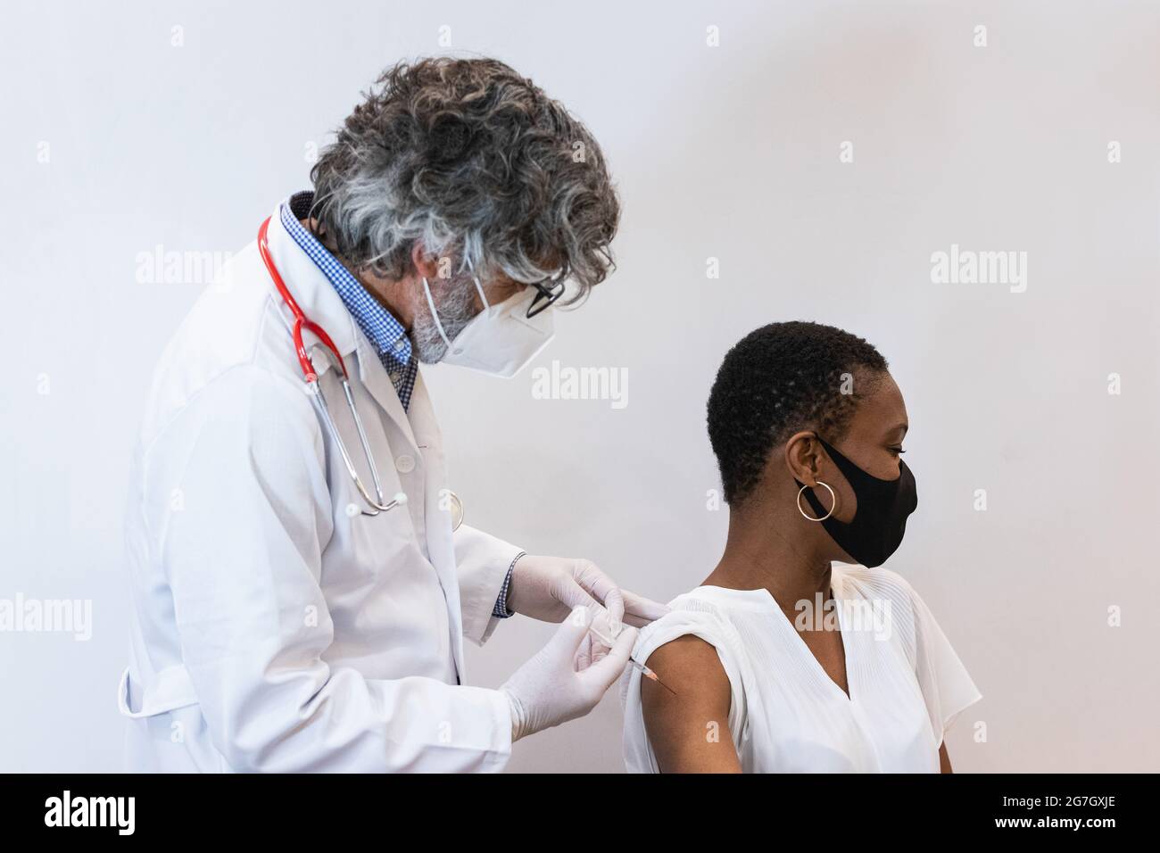 Male medic making injection for black female patient in mask Stock ...