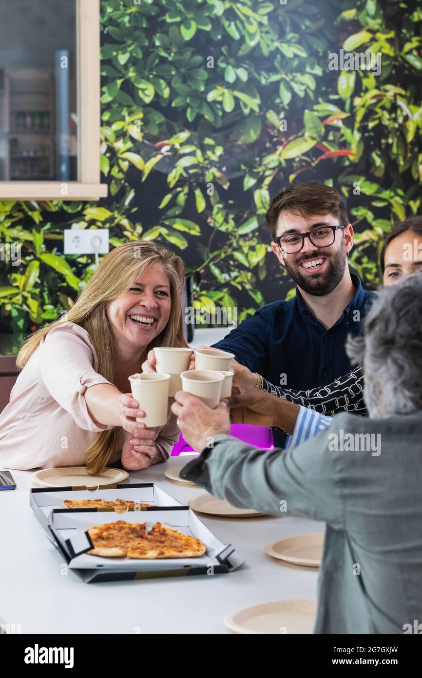 Group of content multiracial coworkers gathering at table and clinking ...