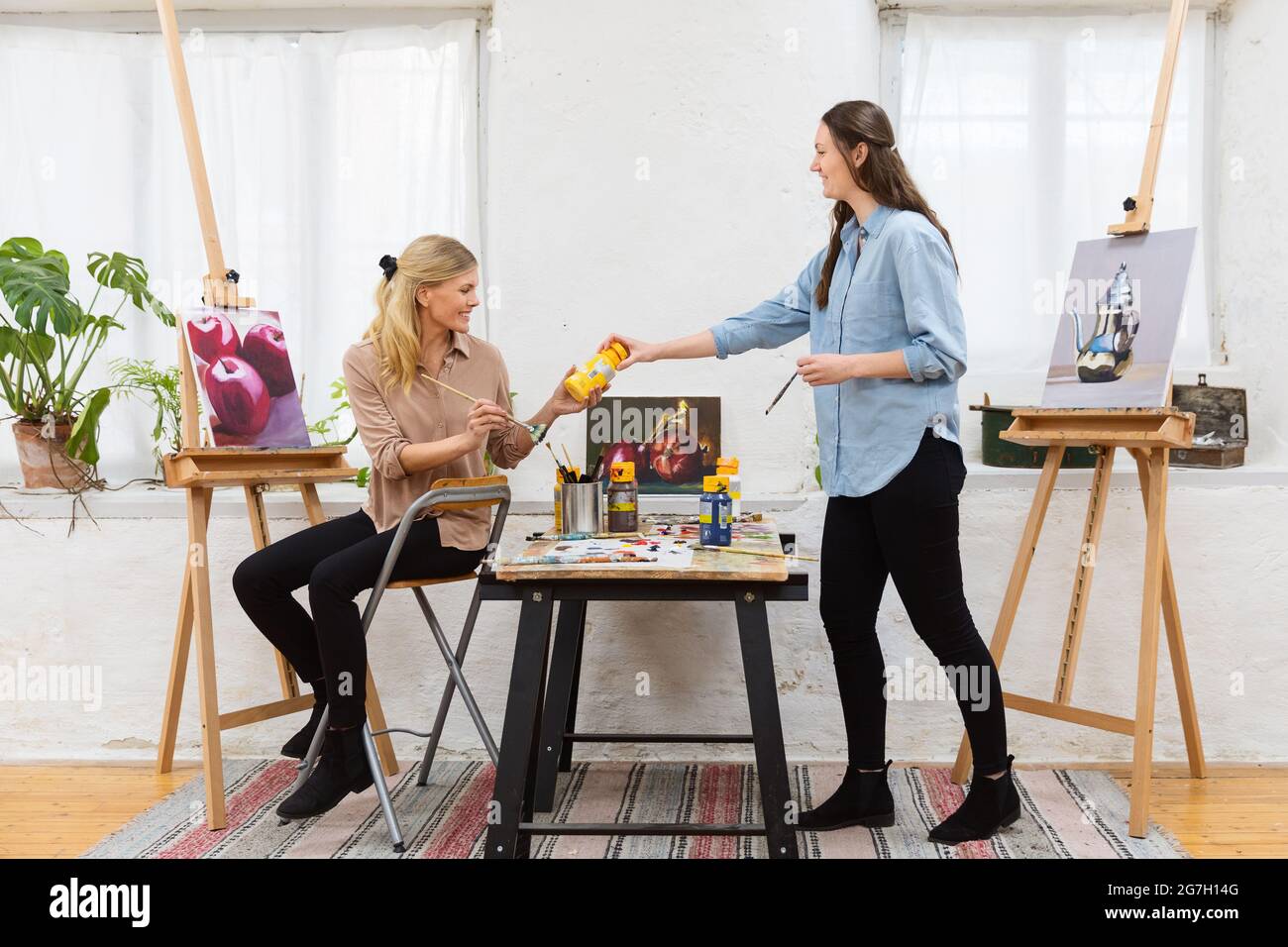 Side view of smiling Woman passing paint for female friend during ...